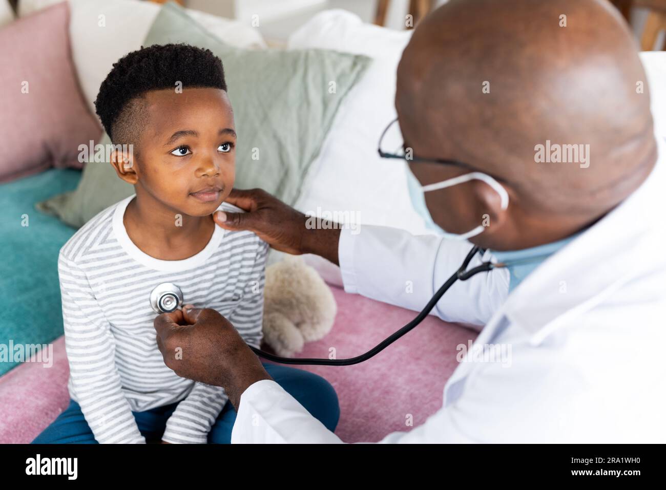 Senior african american male doctor in face mask examining boy patient ...