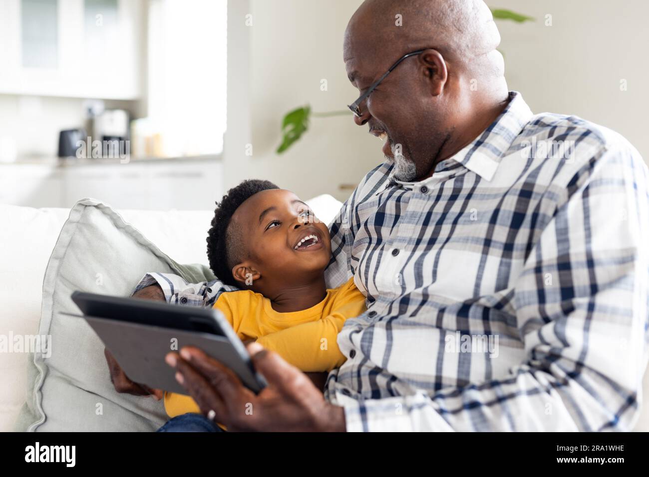 Happy african american grandfather and grandson sitting on sofa and ...