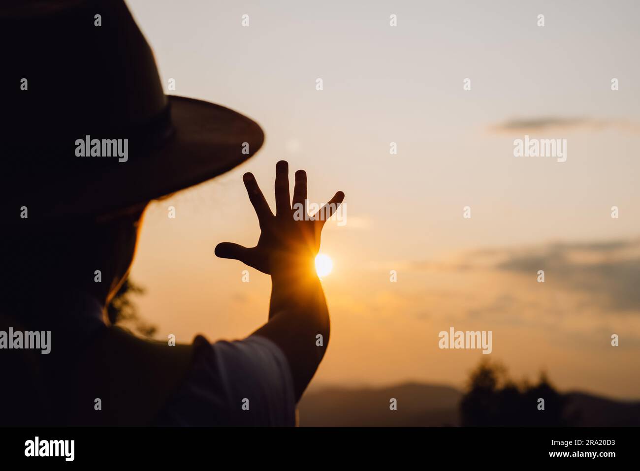 Little girl in hat raising hand over sunset sky, enjoying life and ...