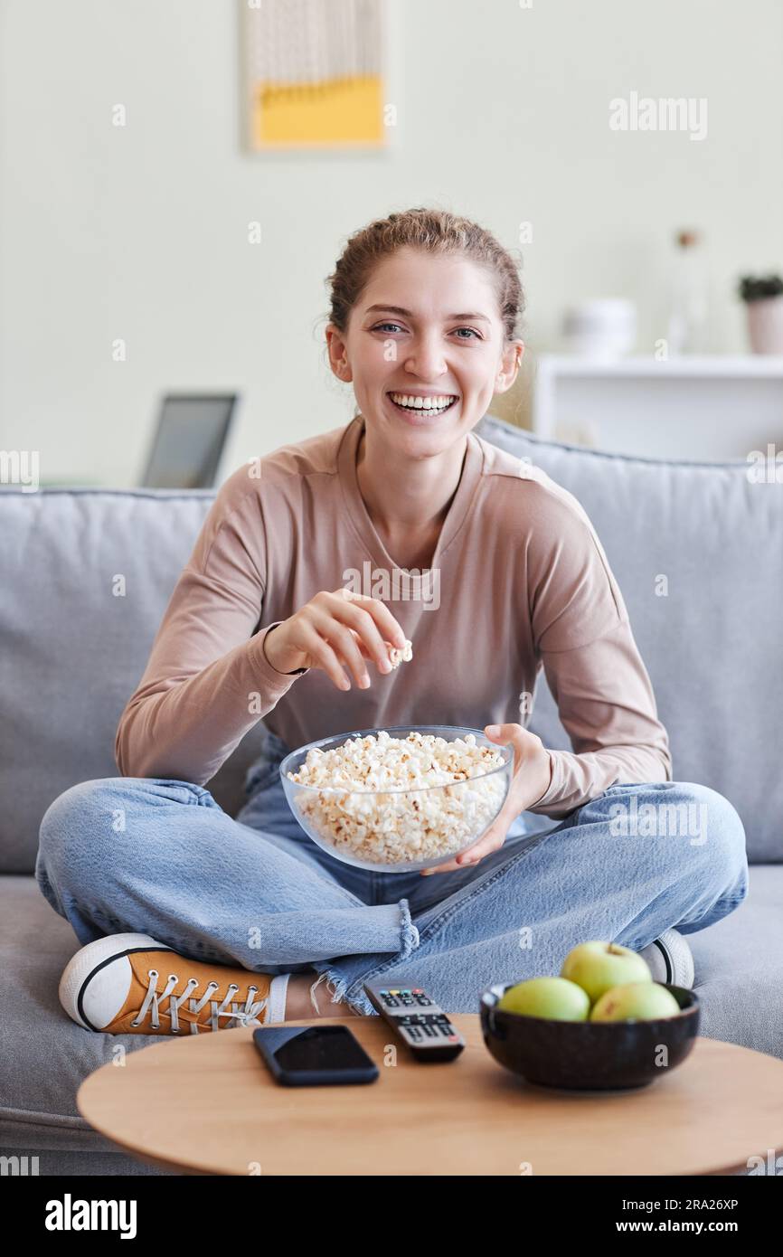 Vertical portrait of carefree young woman sitting on sofa with legs ...