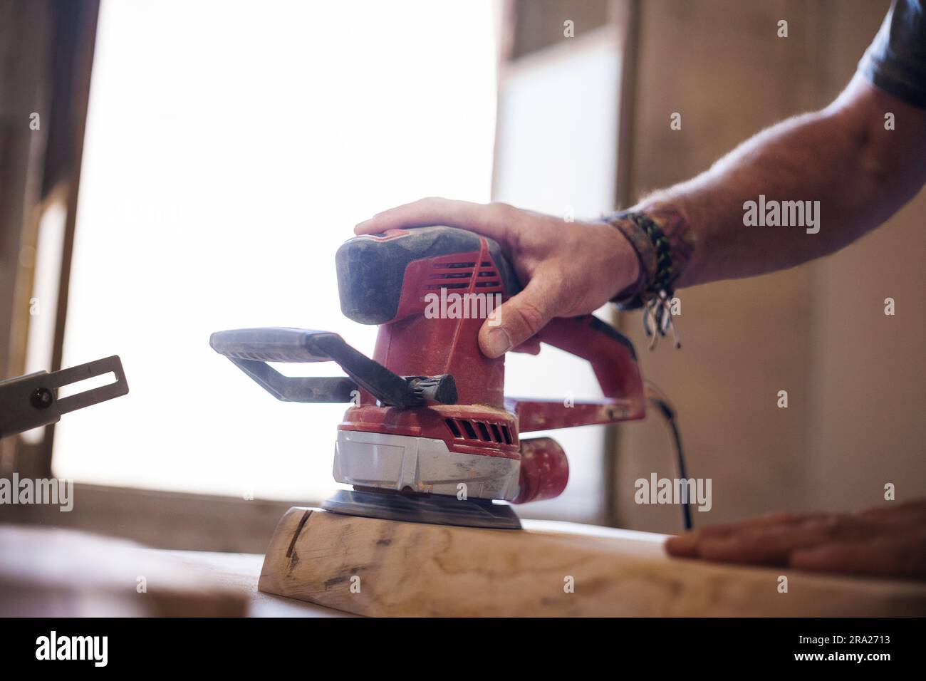 Photo of a carpenter's hand using a sander with natural light coming ...