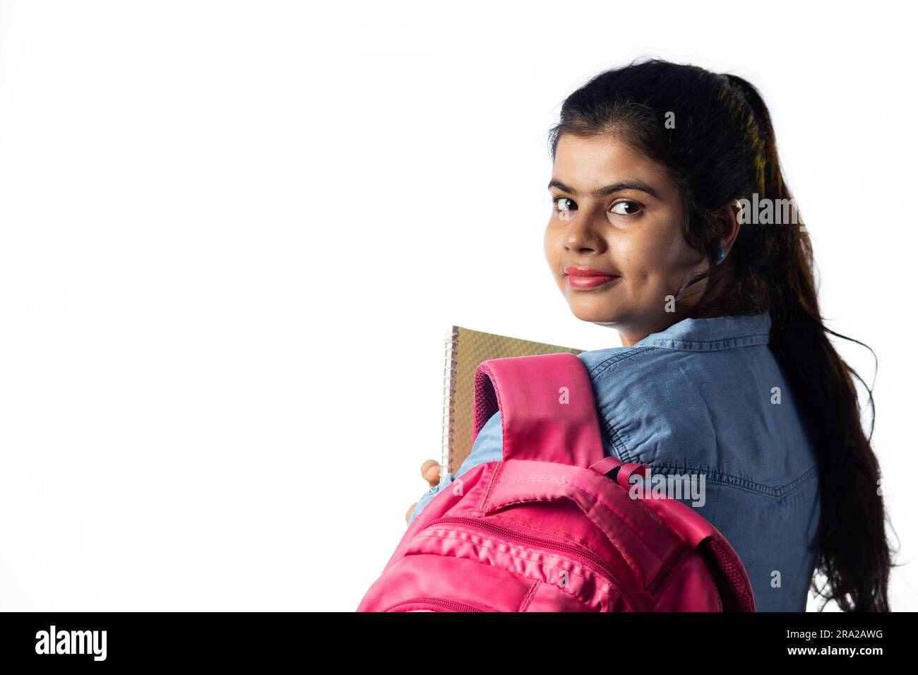 A pretty young Indian girl with books in hand and backpack looking back ...