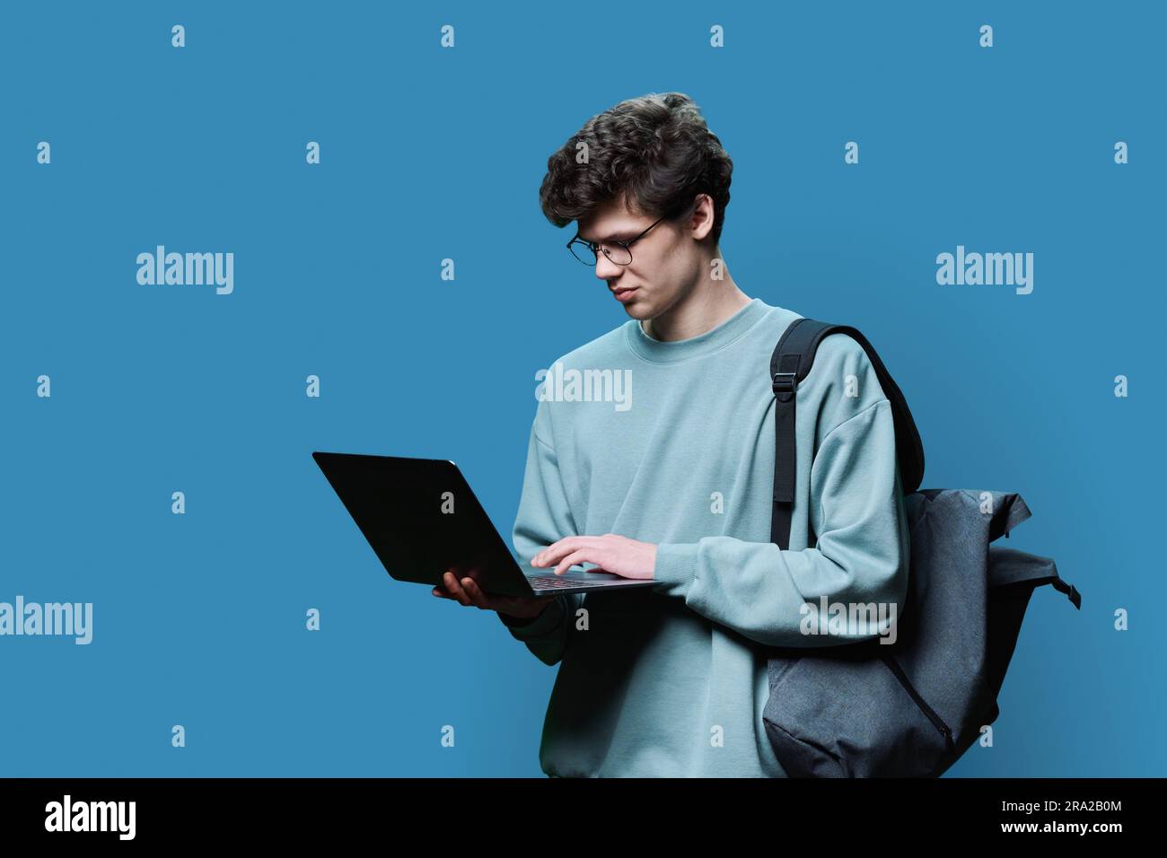 Young male college student using laptop, blue studio background Stock ...