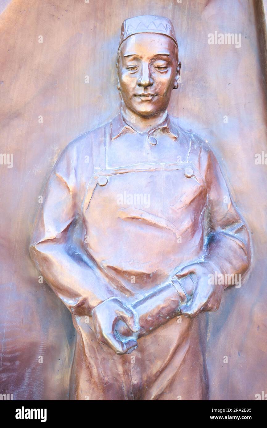 Portrait of a factory worker wearing an apron. Detail of the front entrance bronze frieze. At ...