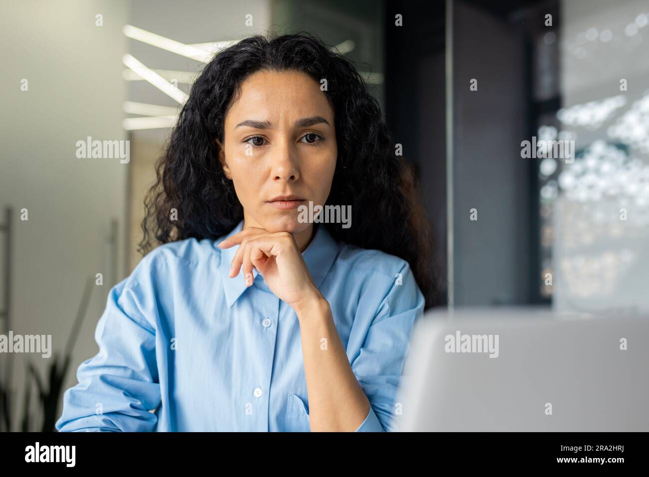 Serious thinking woman working inside office at workplace with laptop ...