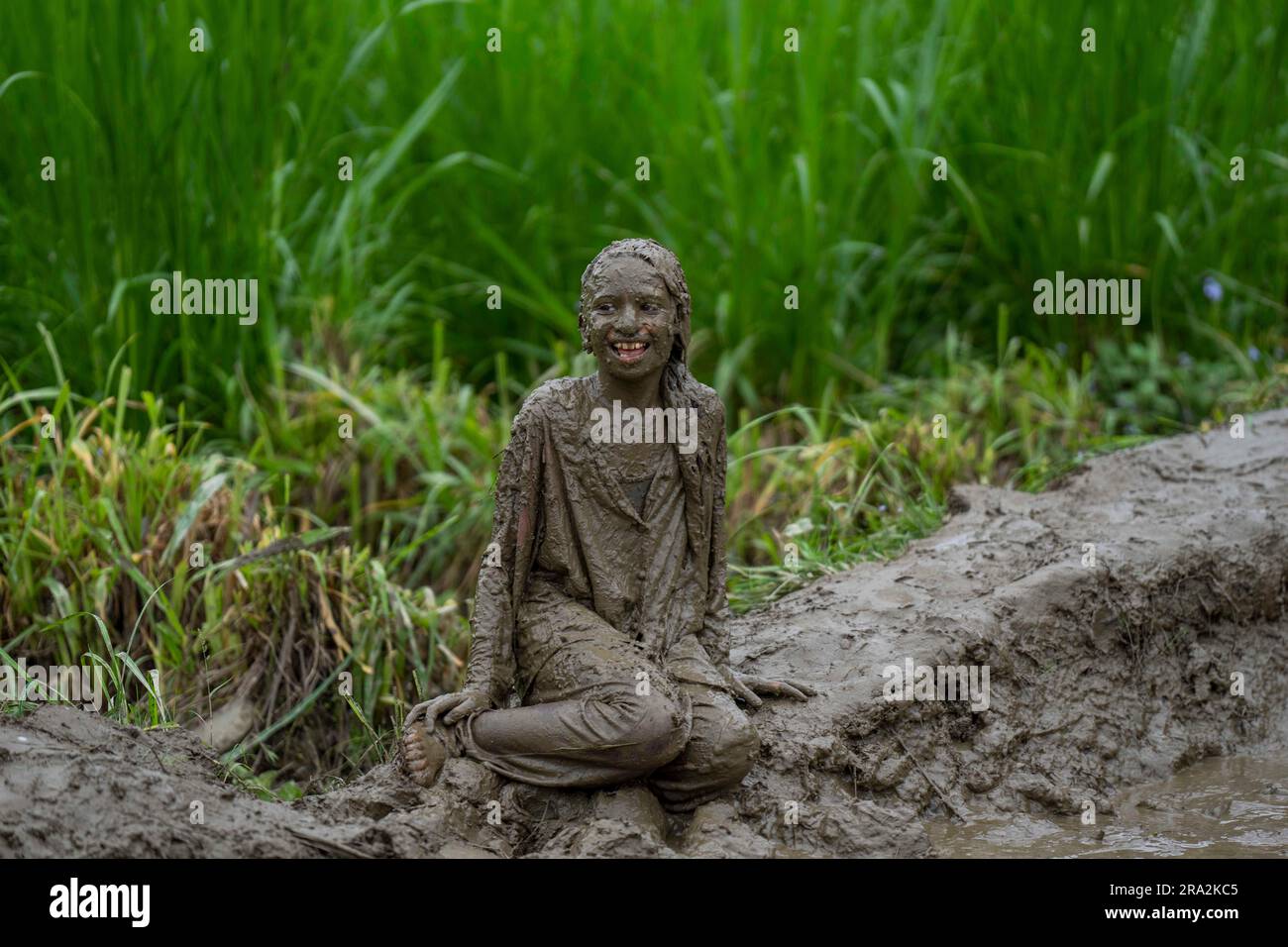 A girl rests while playing with the mud in a paddy field during Asar ...