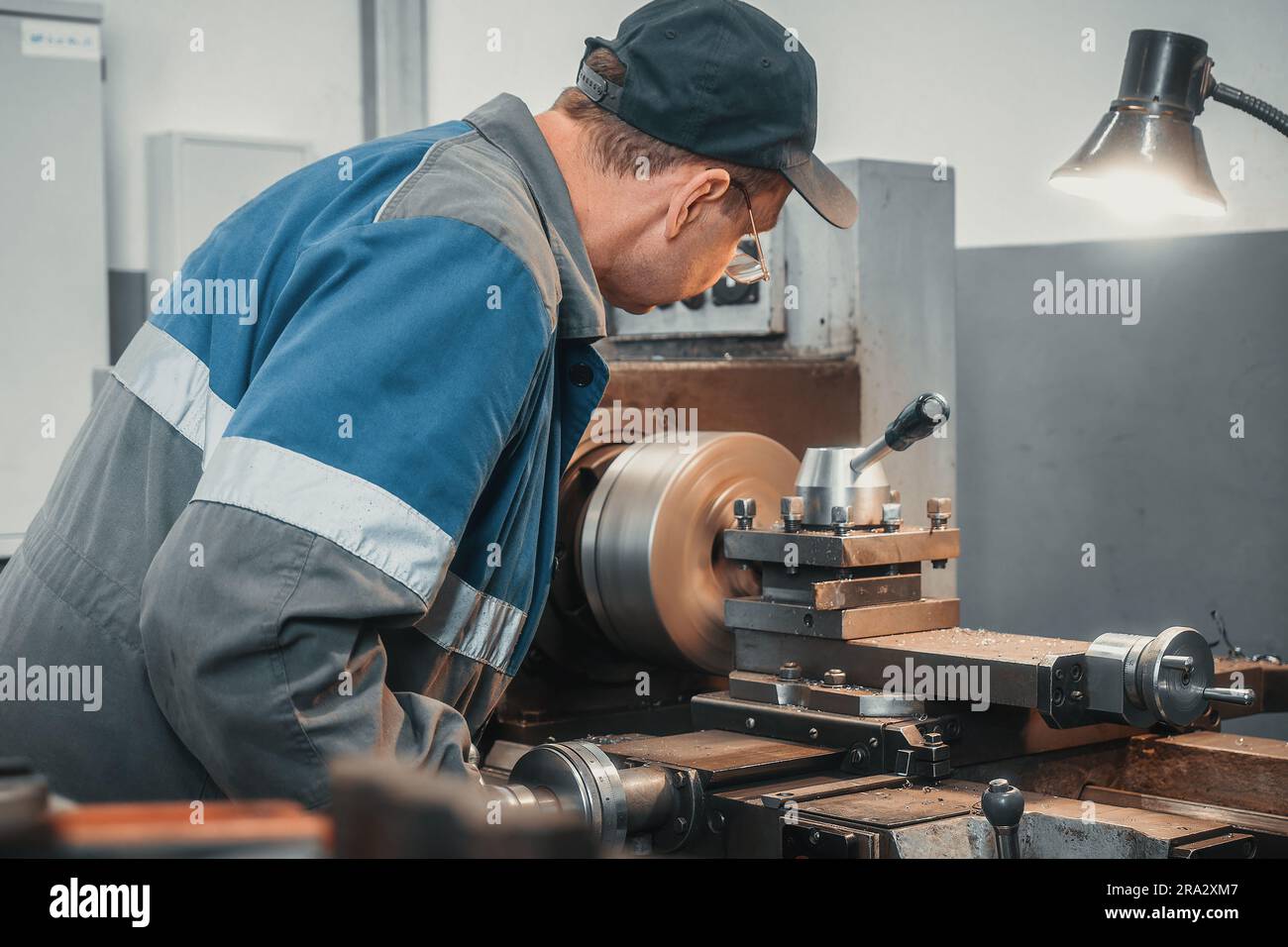 A turner in overalls works on a lathe in a workshop in a factory ...