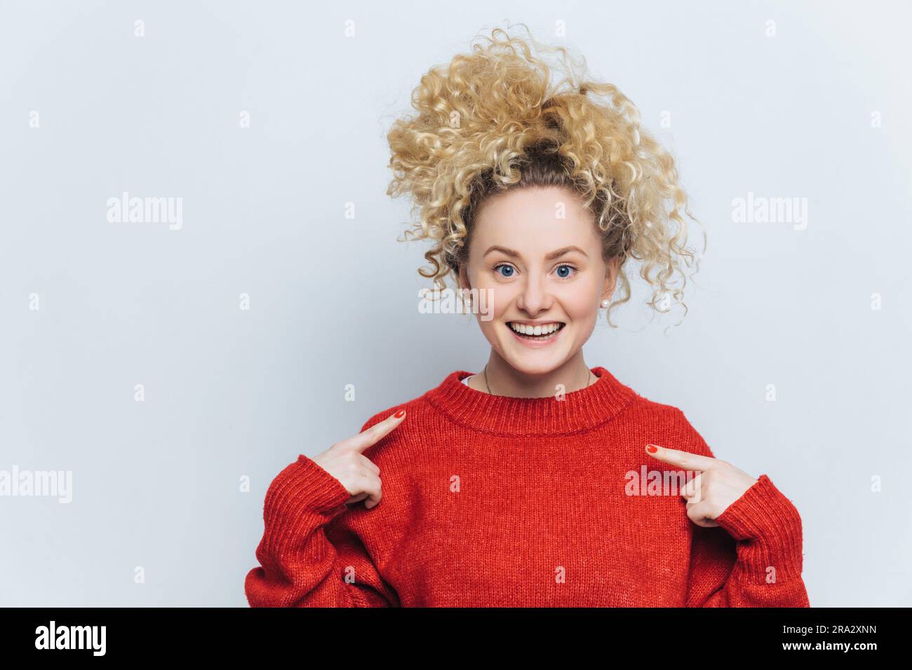 Cheerful woman in red sweater, smiles, points at blank space ...