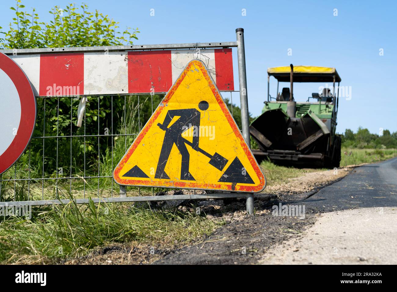 Road work ahead warning sign at construction site. Paver finisher equipment in bg. Crawler ...