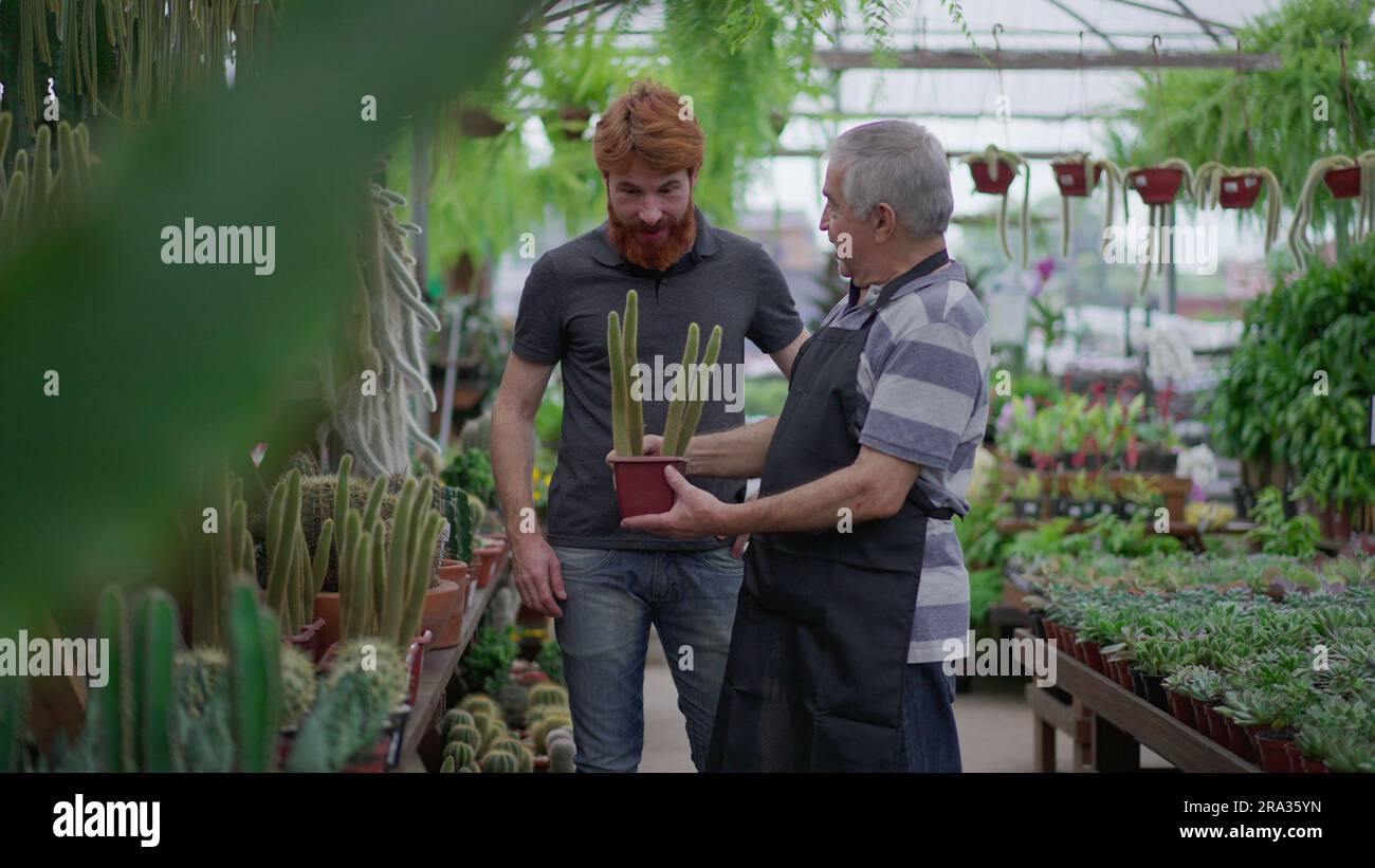 Senior employee helping young customer to buy plants inside ...