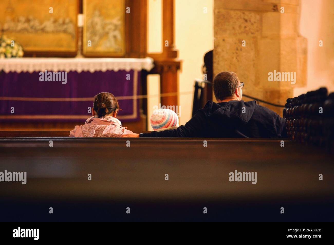 A rear view of a family sitting on the prayer seats inside a church ...