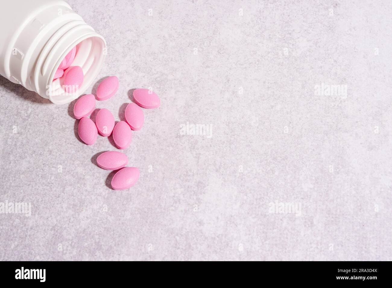 Pink pills pouring out of the white bottle on light concrete background ...