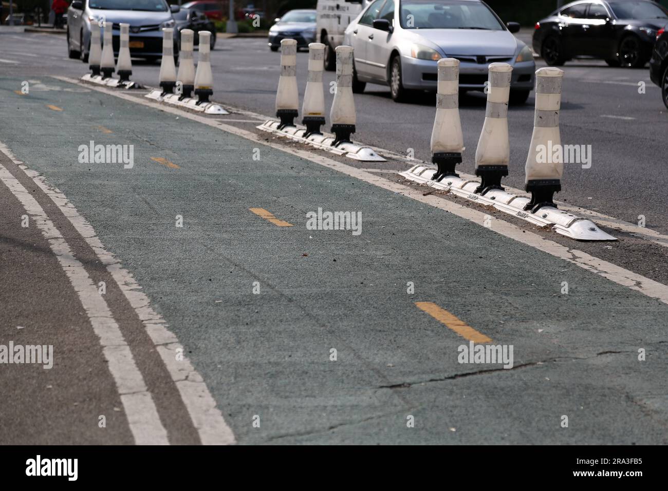 green bike lane painted on street next to cars with safety poles ...