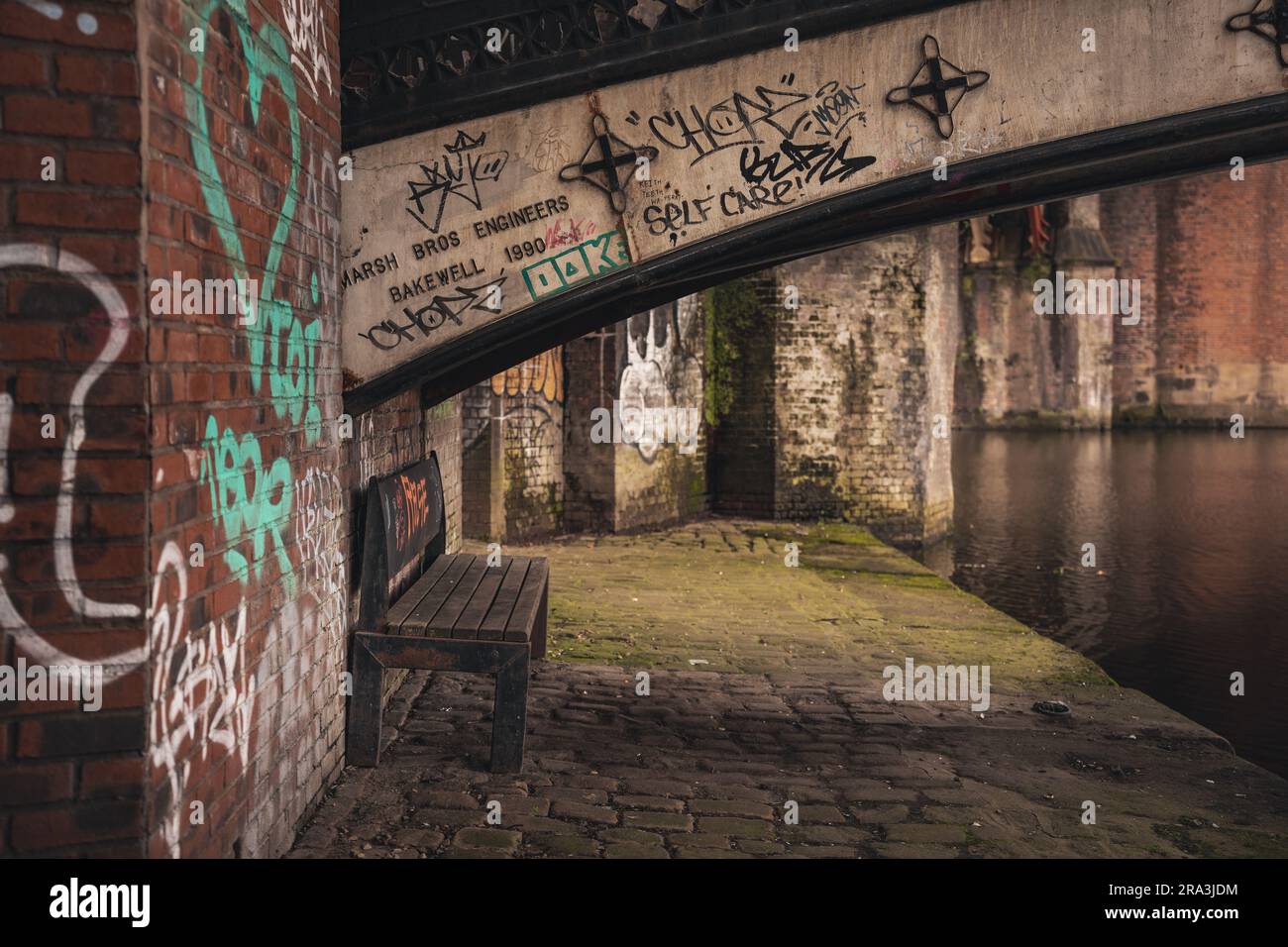 A graffiti-covered bridge situated next to a river and brick wall Stock ...