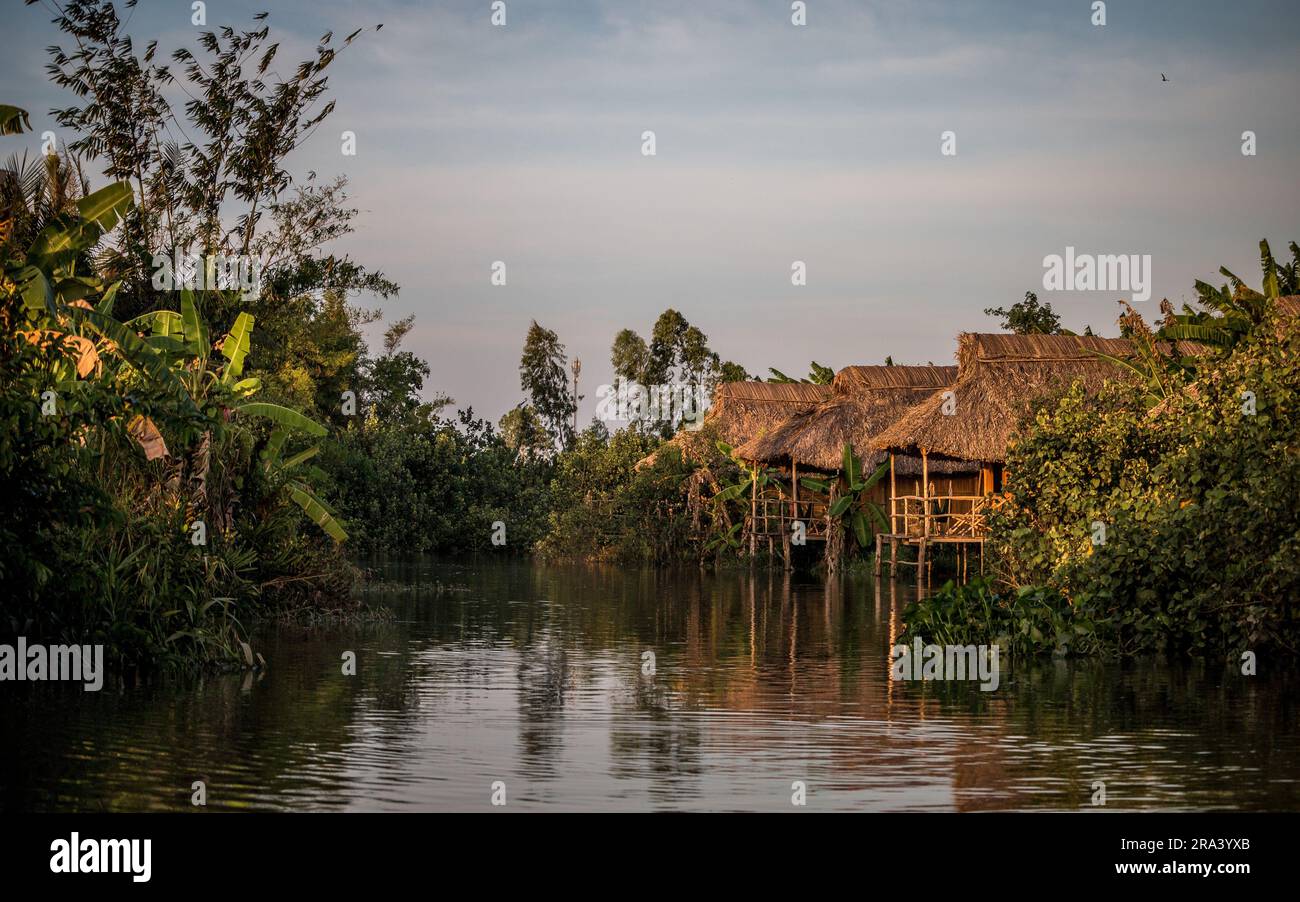 A scenic view of traditional bamboo huts along the side of a river in a ...