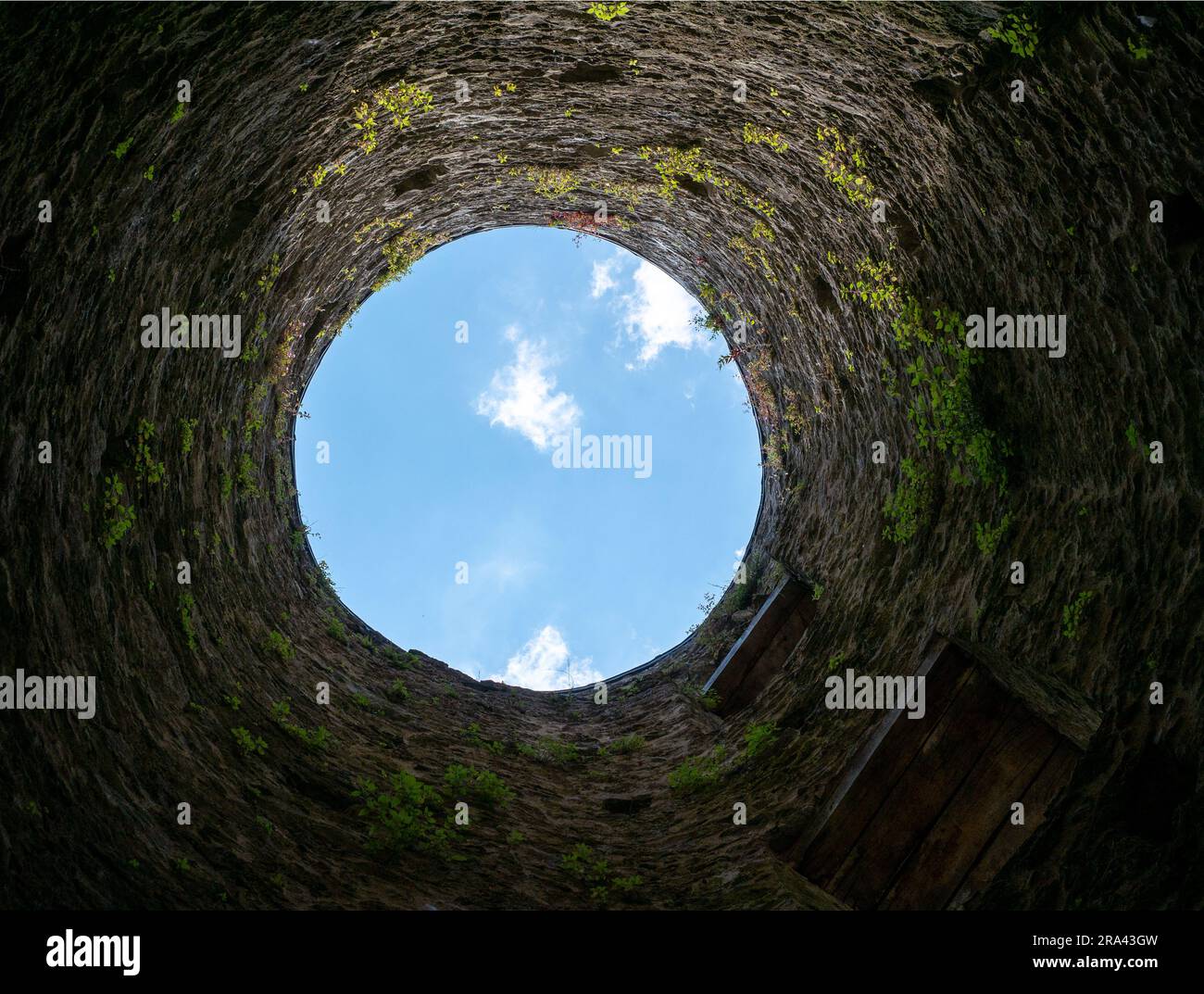 Stone well hole, old construction from inside, brick walls and blue sky ...