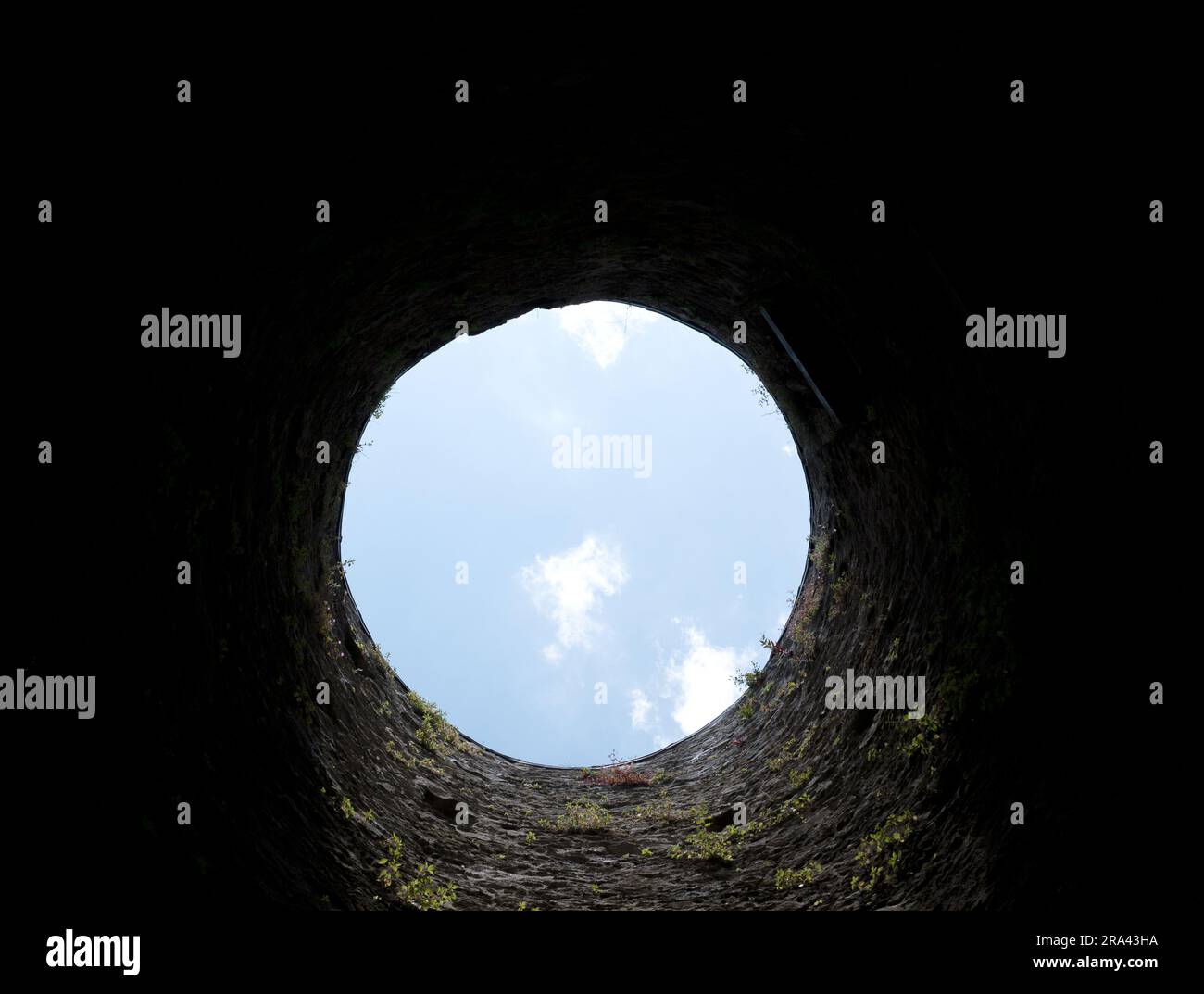 Stone well hole, old construction from inside, brick walls and blue sky ...