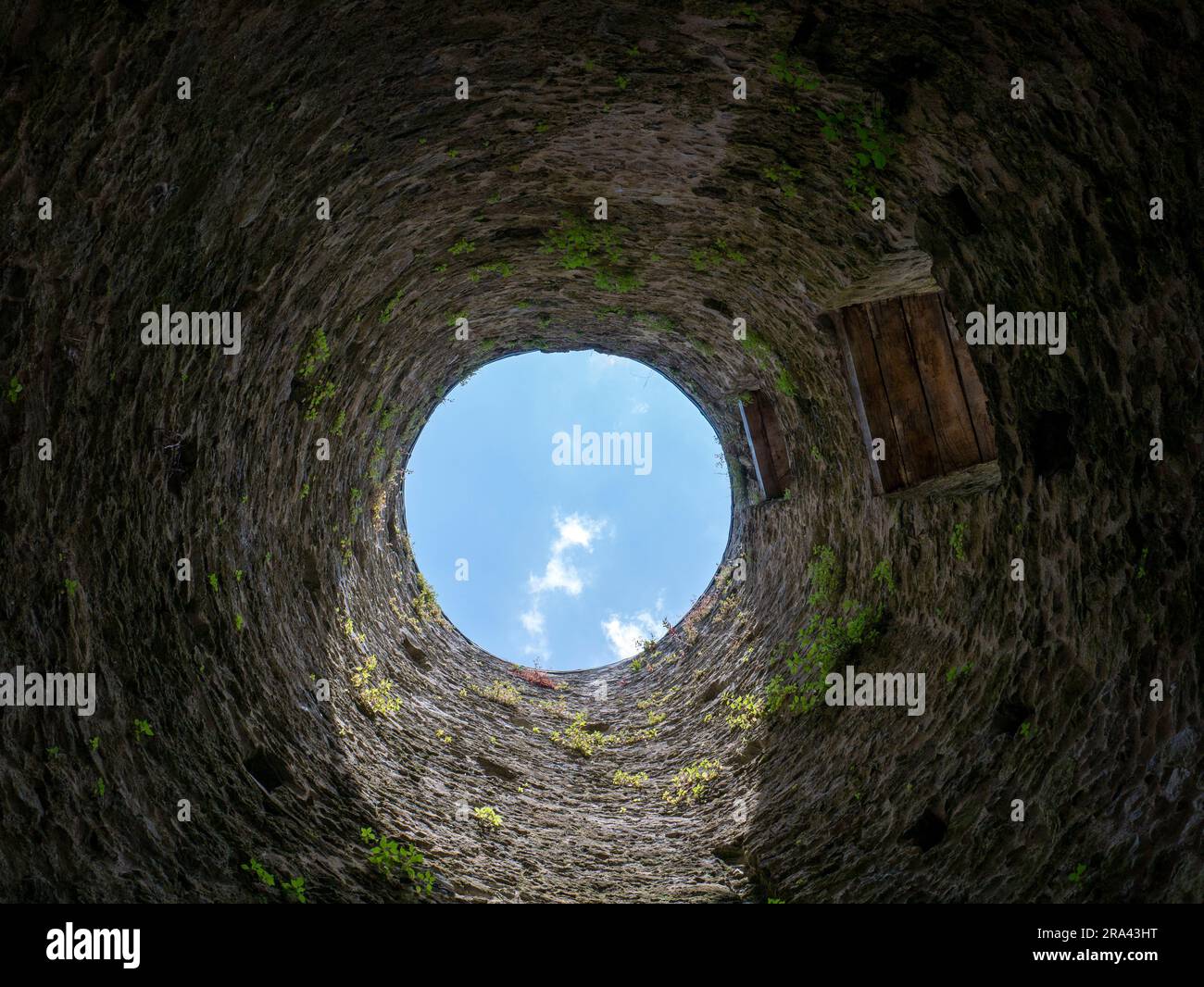 Stone well hole, old construction from inside, brick walls and blue sky ...