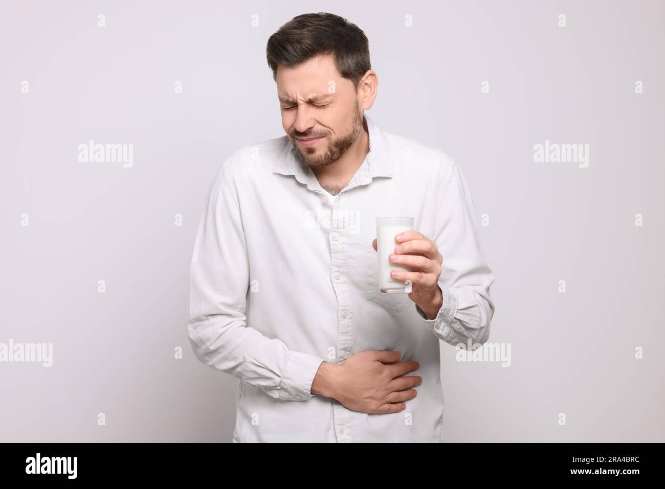 Man with glass of milk suffering from lactose intolerance on white ...
