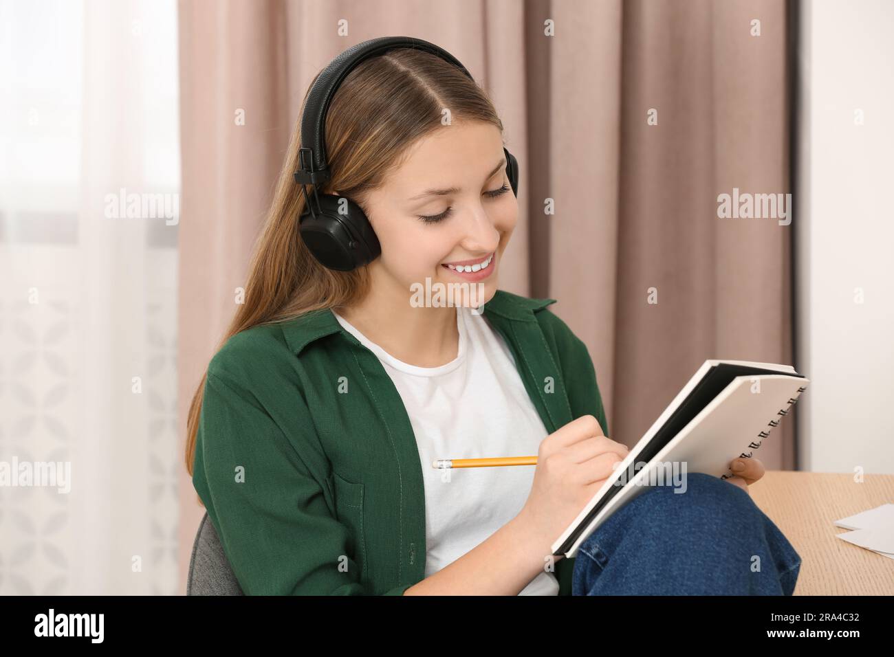 Teenage girl with headphones writing in notebook indoors Stock Photo ...