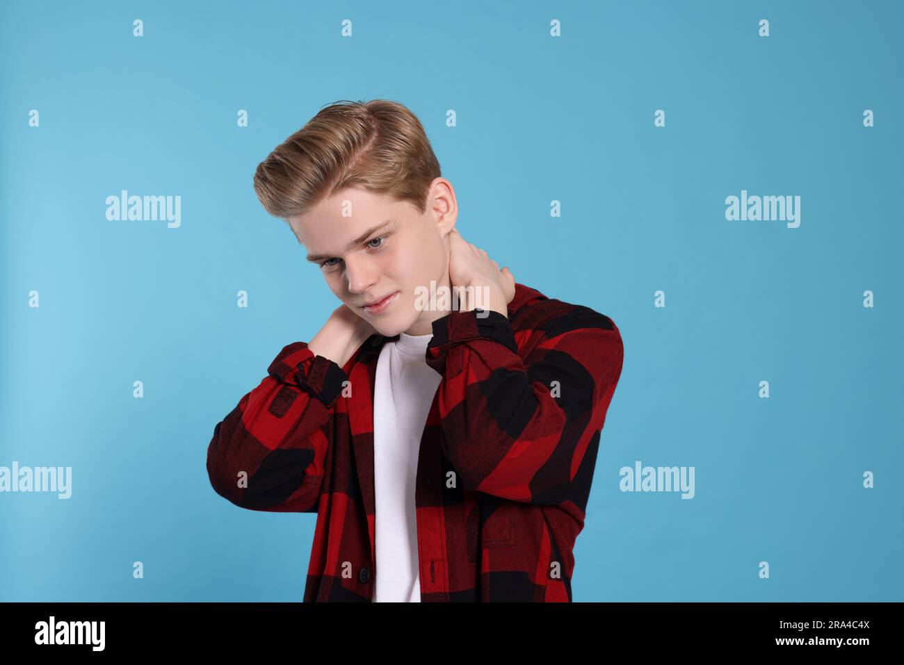 Teenage boy suffering from pain in neck on light blue background ...