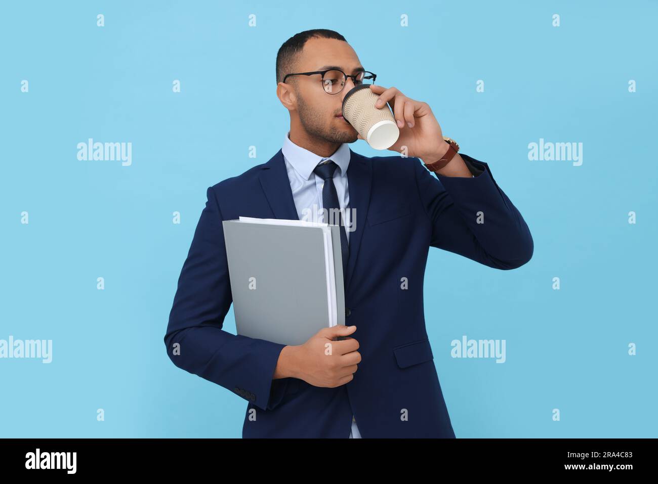 Young intern with notebooks drinking hot coffee on light blue ...