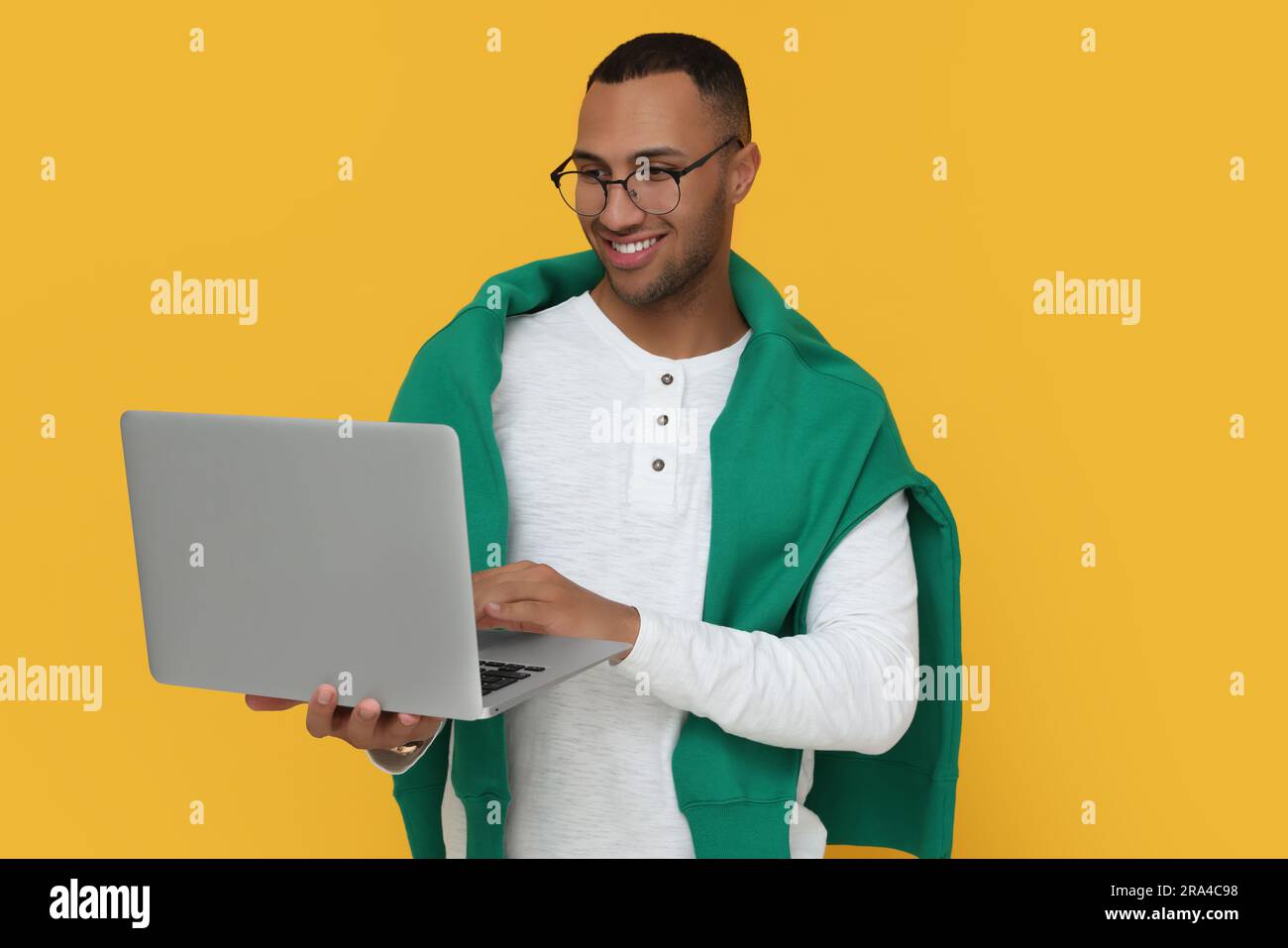 Happy young intern holding laptop on orange background Stock Photo - Alamy