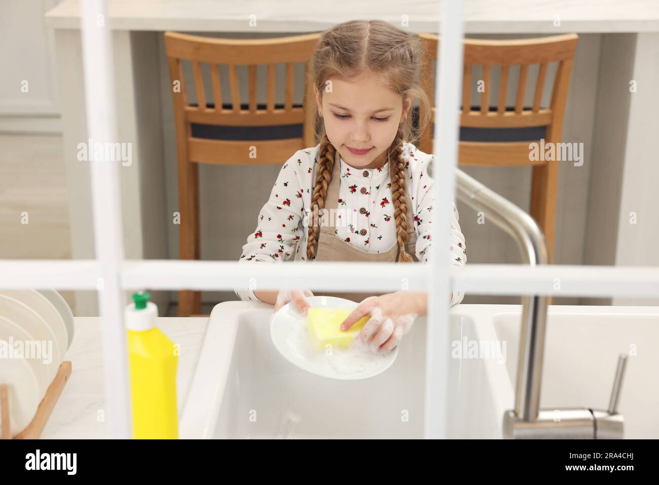 Little girl washing plate above sink indoors, view from outside Stock ...