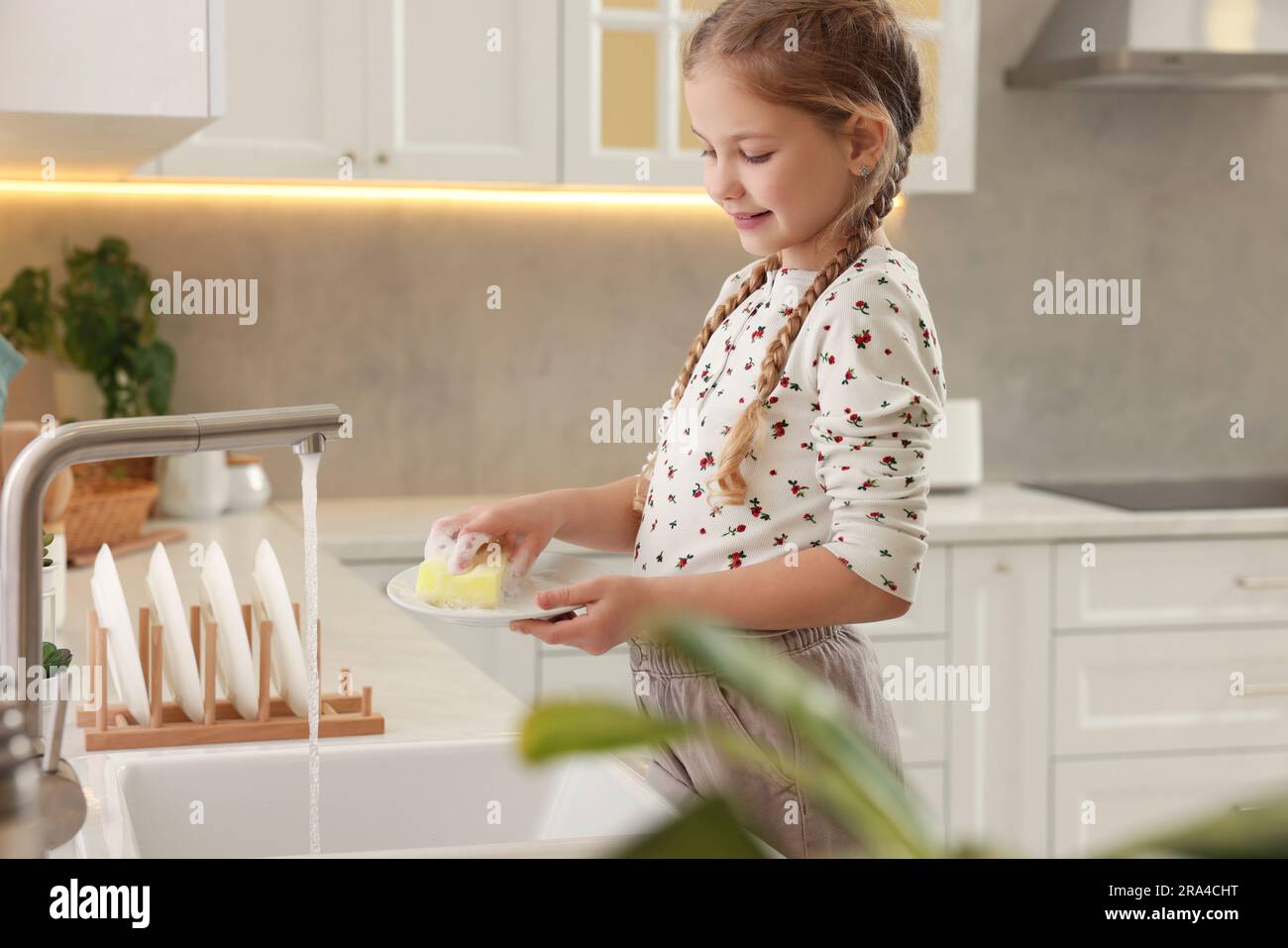 Little girl washing plate above sink in kitchen Stock Photo - Alamy