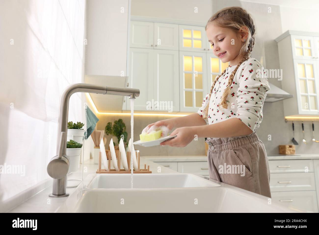 Little girl washing plate above sink in kitchen Stock Photo - Alamy