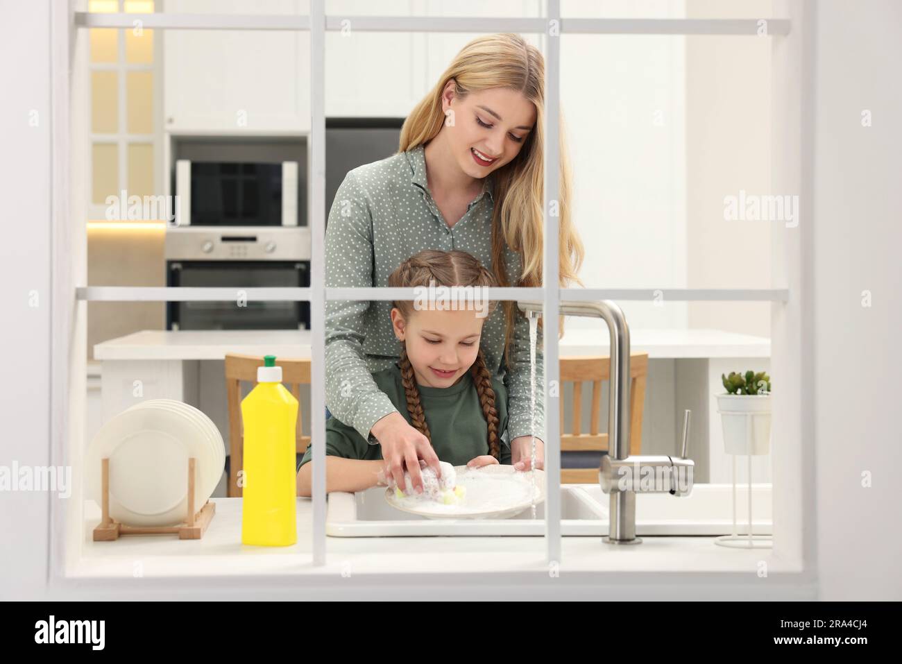 Mother and daughter washing plate above sink in kitchen, view from ...