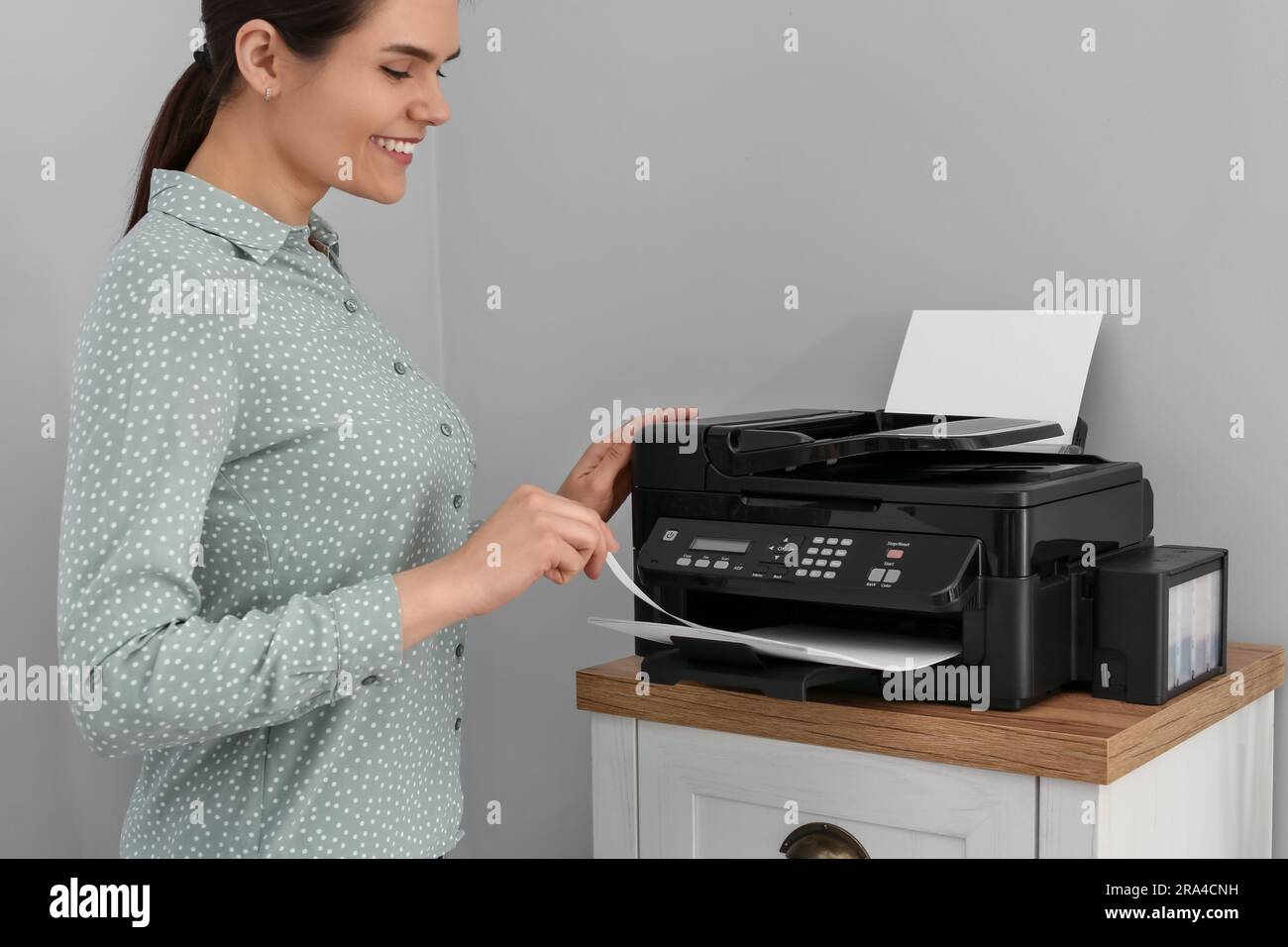 Woman using modern printer on chest of drawers at home Stock Photo - Alamy