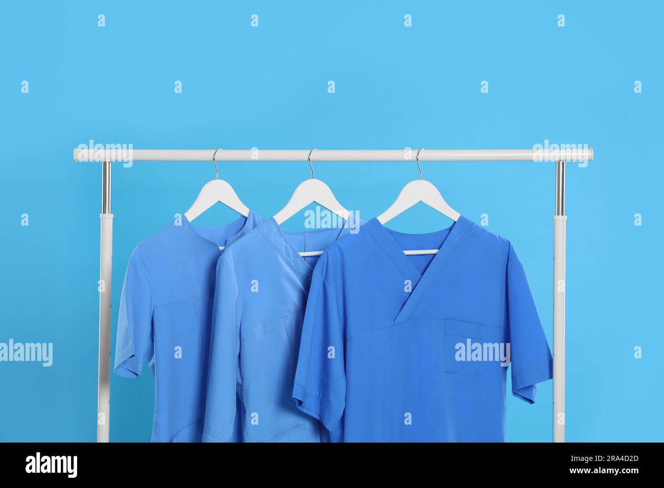 Medical uniforms on rack against light blue background Stock Photo - Alamy