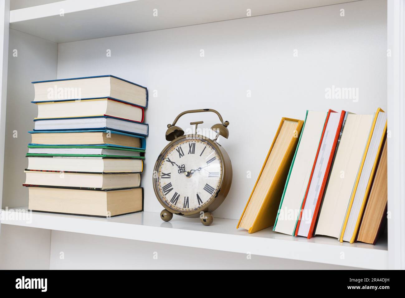 Different books and alarm clock on shelving unit Stock Photo - Alamy