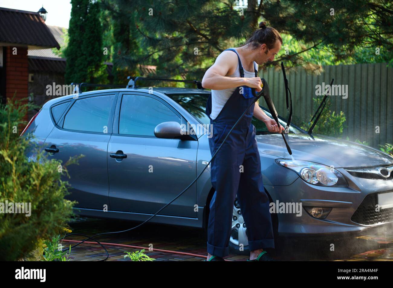 Young car service worker in blue uniform, directs sprayer at headlight ...