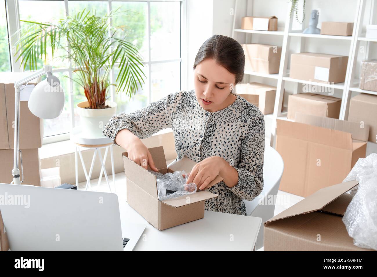 Young woman packing parcel for client in office Stock Photo - Alamy