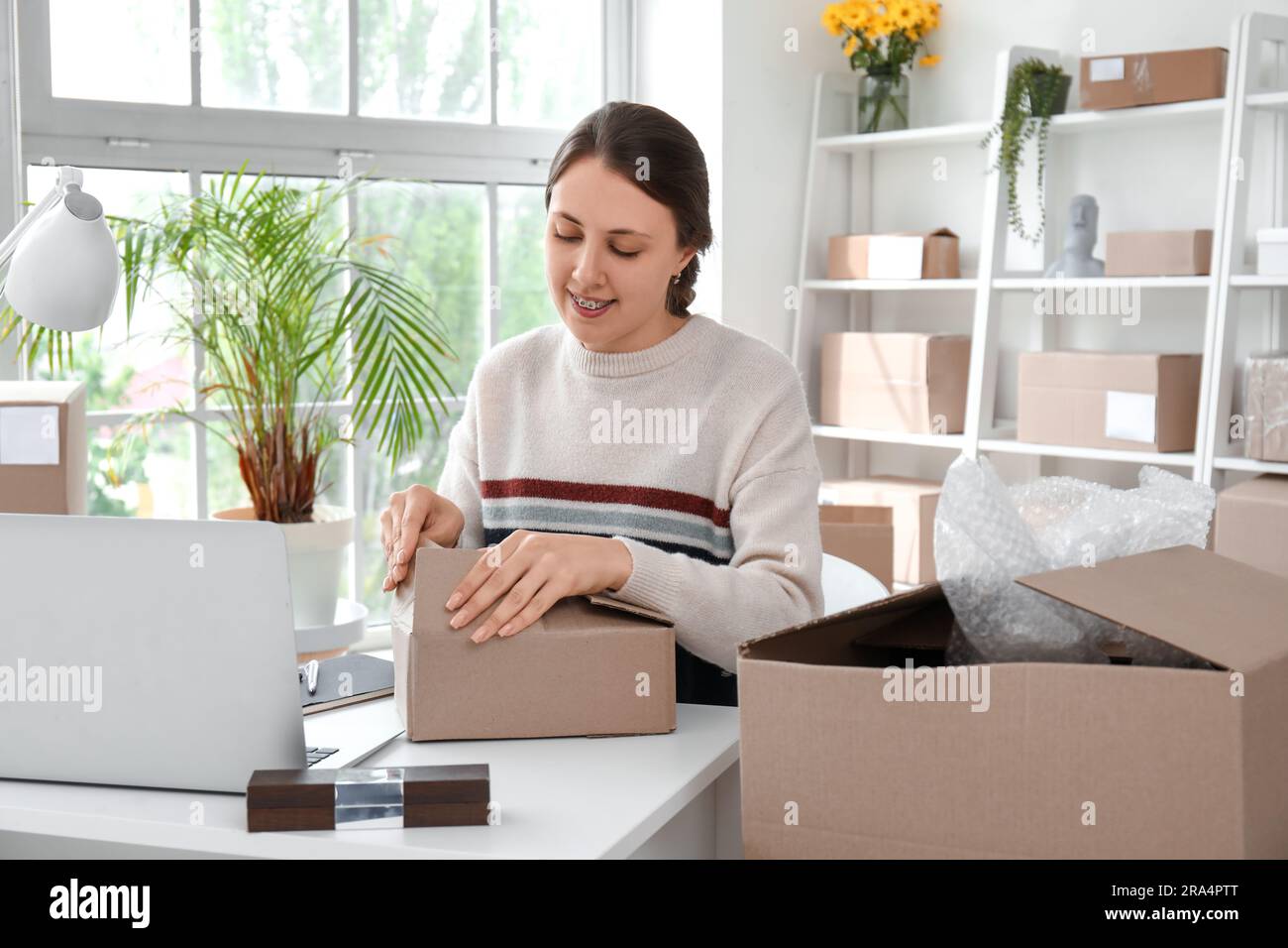 Young woman packing parcel for client in office Stock Photo - Alamy