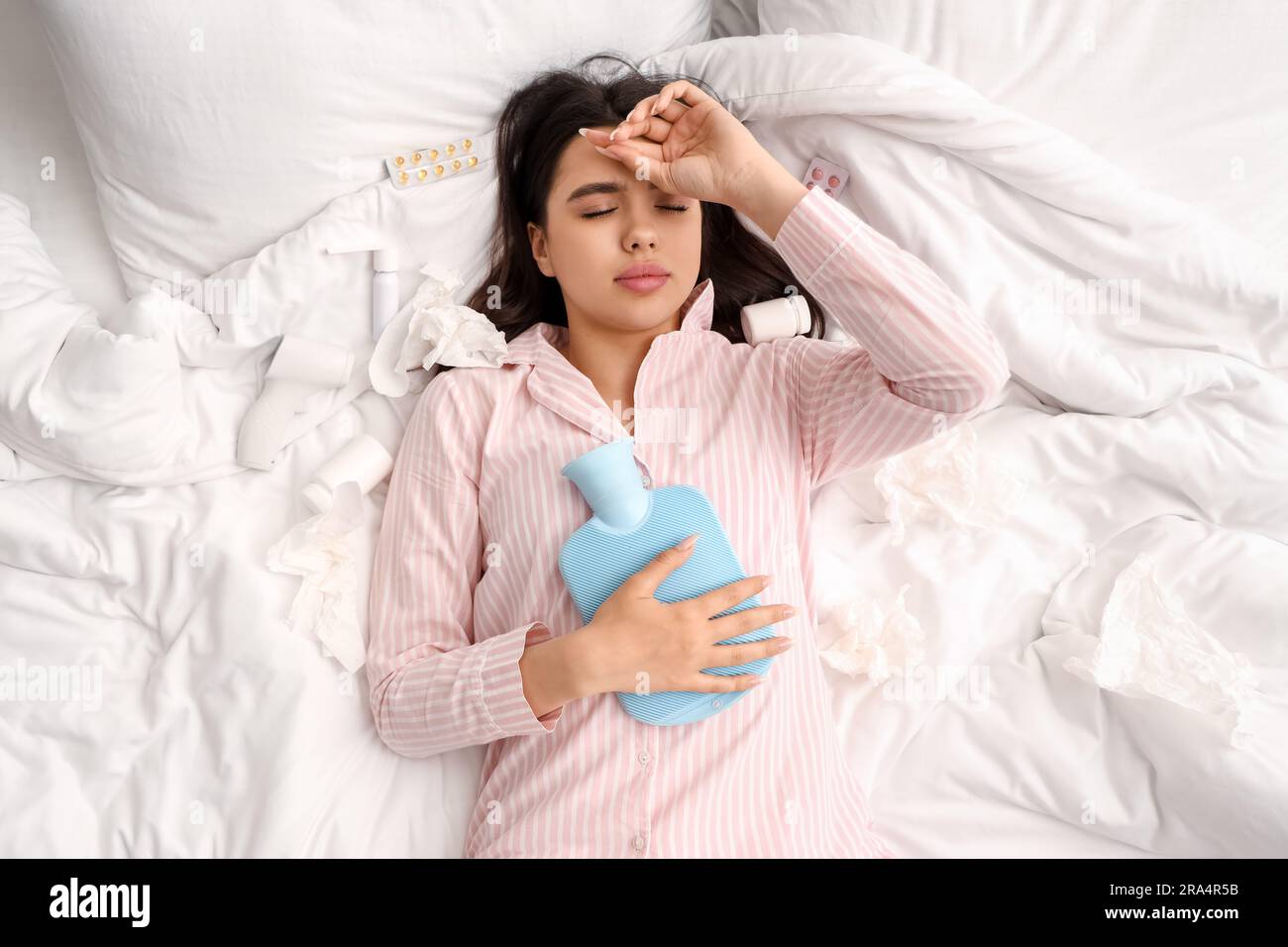 Sick young woman with hot-water bag in bed, top view Stock Photo - Alamy