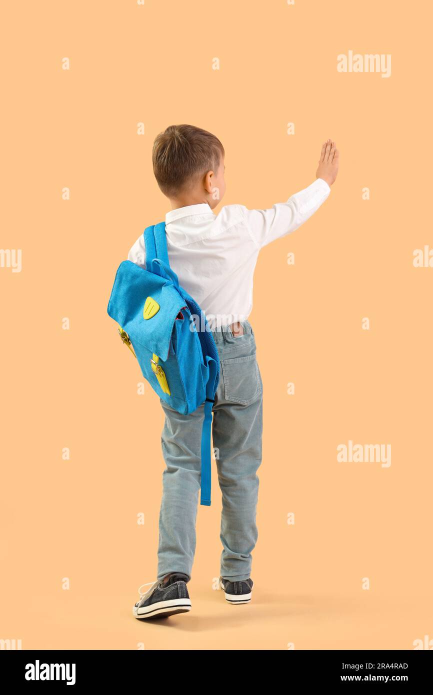 Little schoolboy with backpack waving hand on orange background, back ...