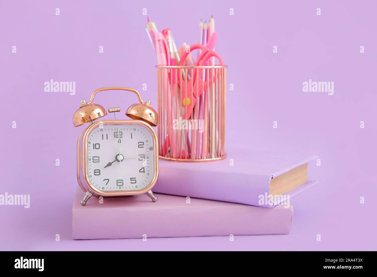 Alarm clock with books and stationery holder on lilac background Stock ...