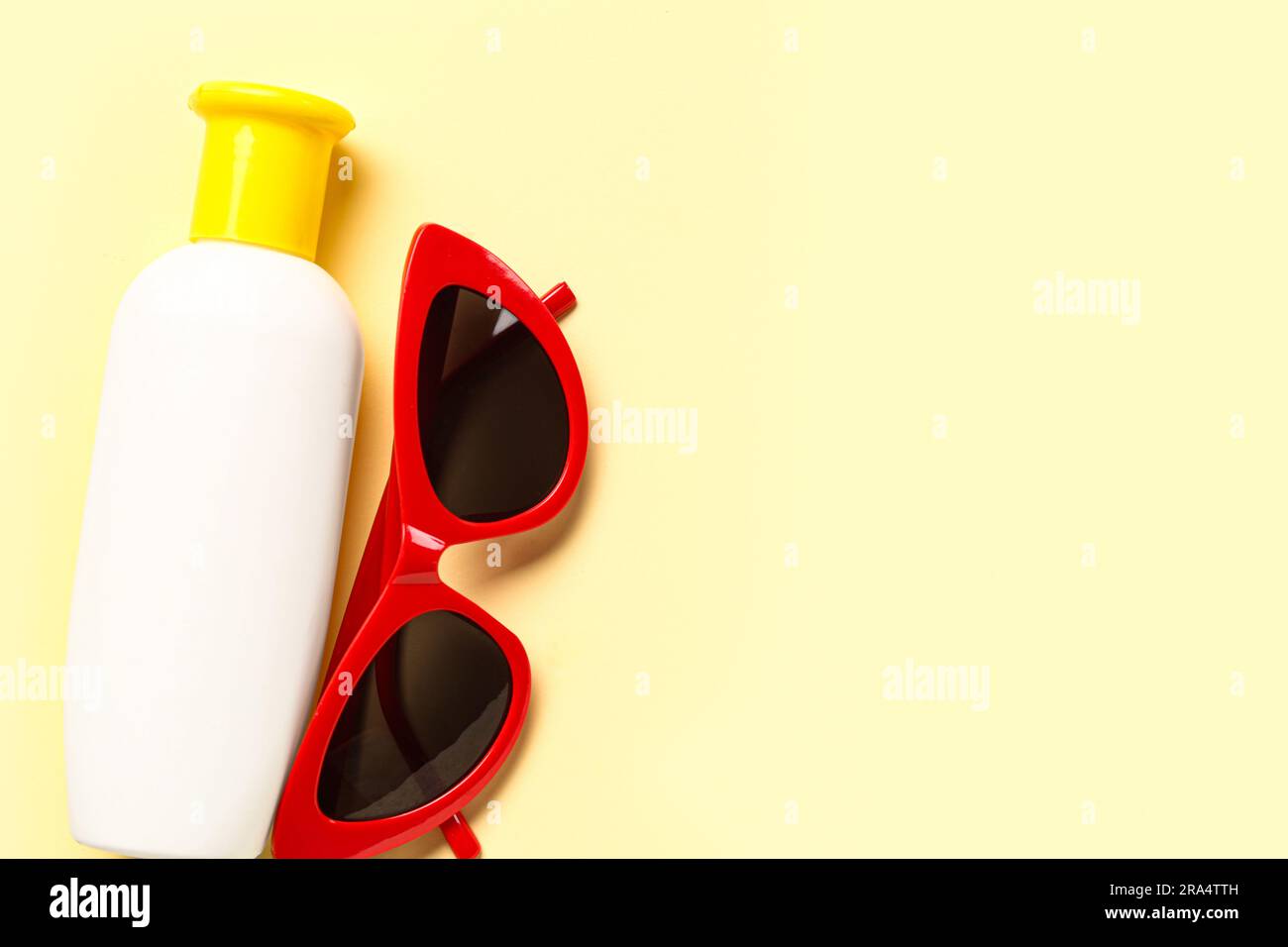 Sunglasses with bottle of sunscreen cream on pale yellow background ...