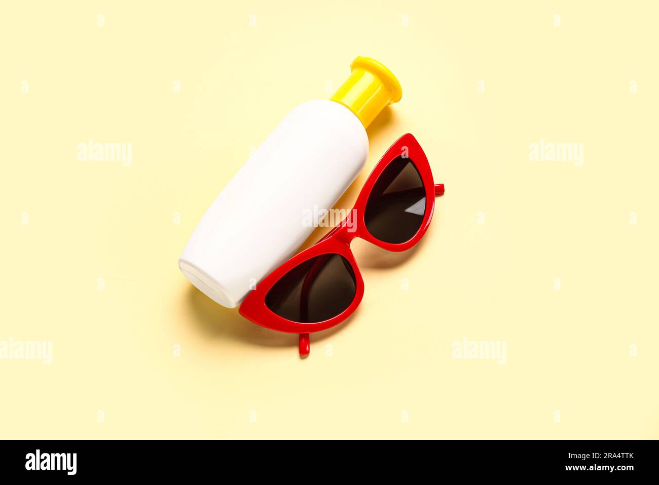 Sunglasses with bottle of sunscreen cream on pale yellow background ...