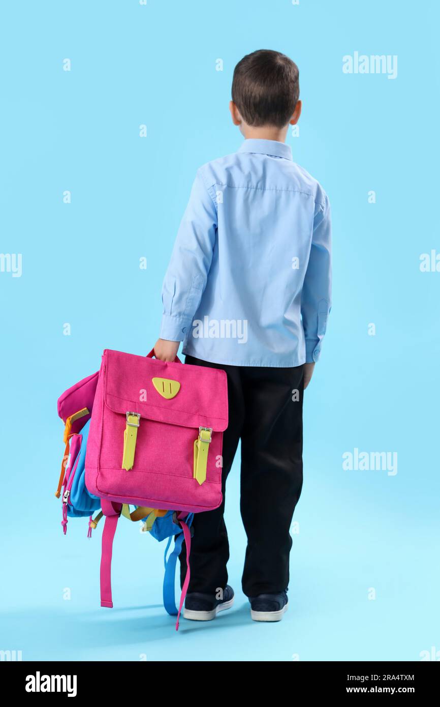 Little schoolboy with backpacks on light blue background, back view ...