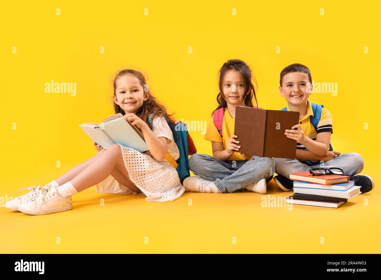Little schoolchildren reading books on yellow background Stock Photo ...