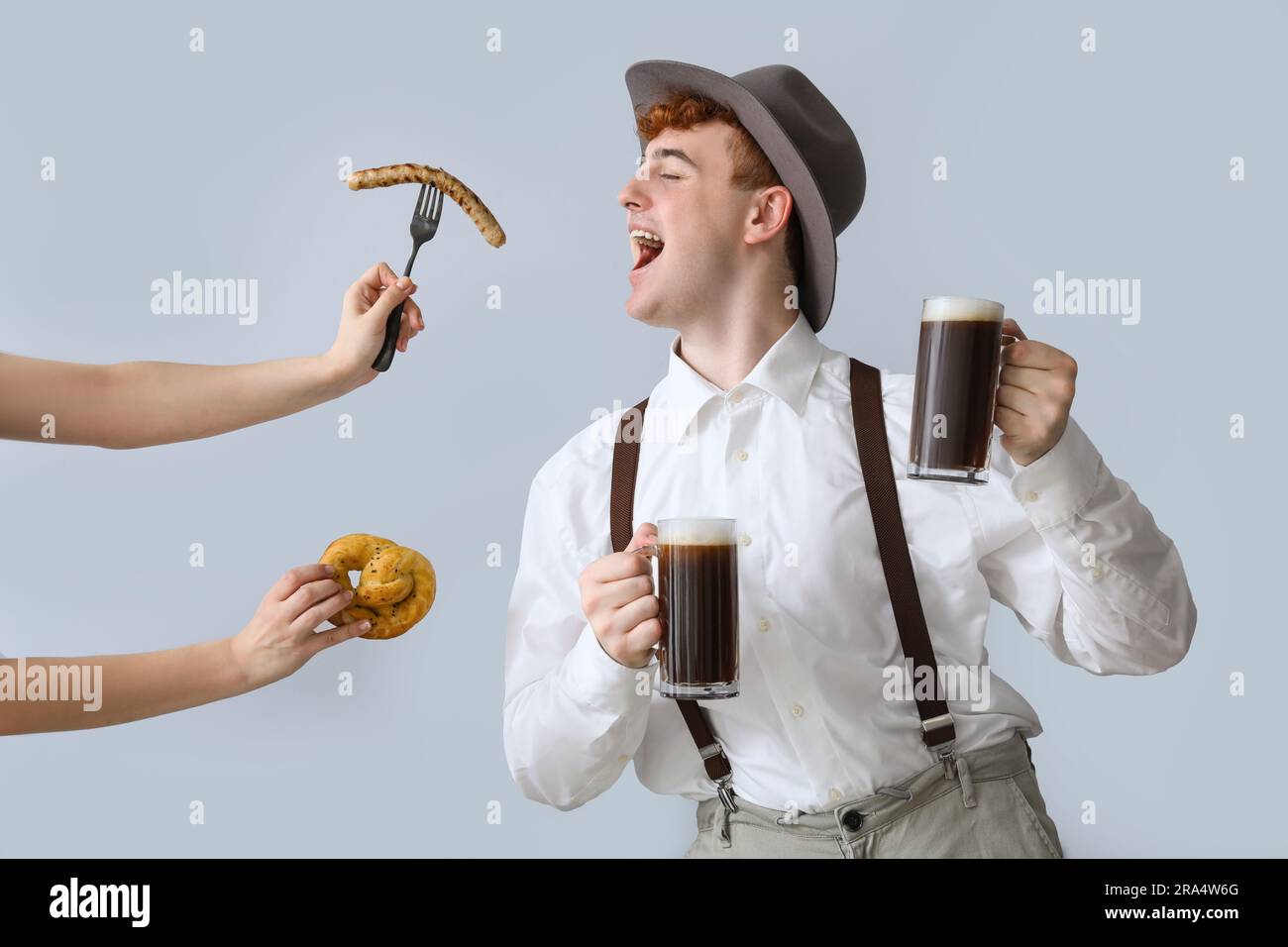 Young man in traditional German clothes and female hands with snacks on ...