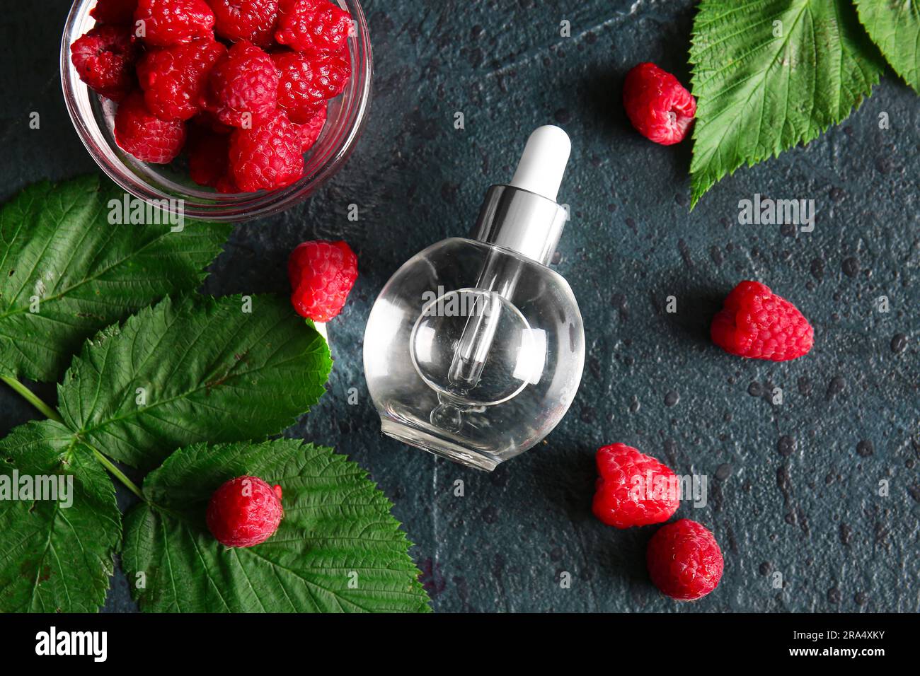 Bottle of cosmetic raspberry oil and bowl with berries on dark ...