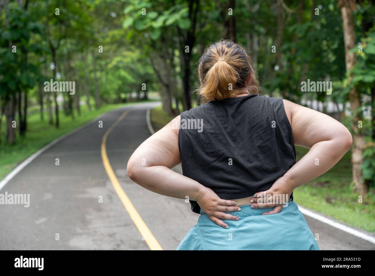 Back view of an overweight woman with back pain putting both hands over ...