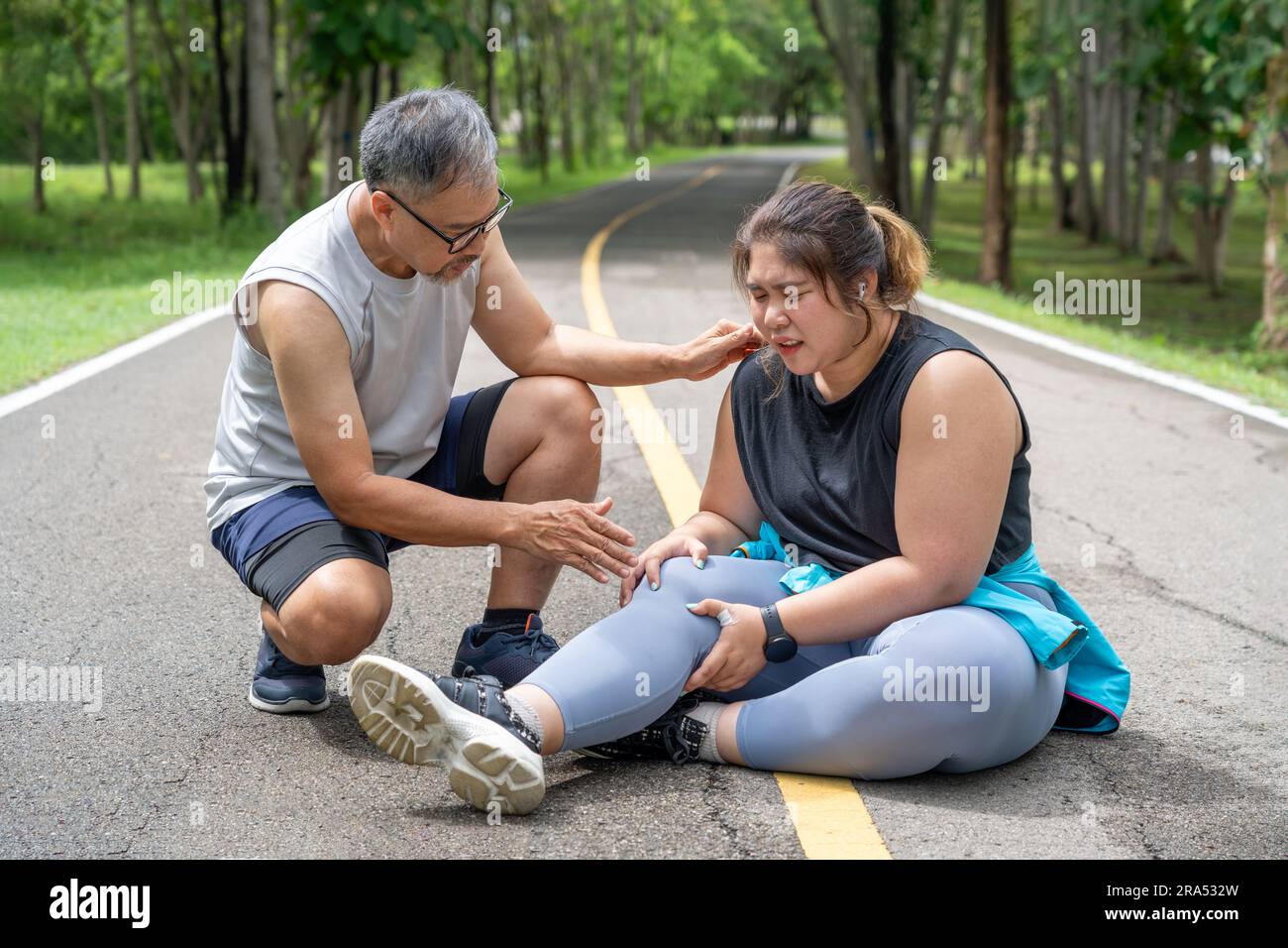 Overweight young woman with injured knee sitting in pain on the running ...
