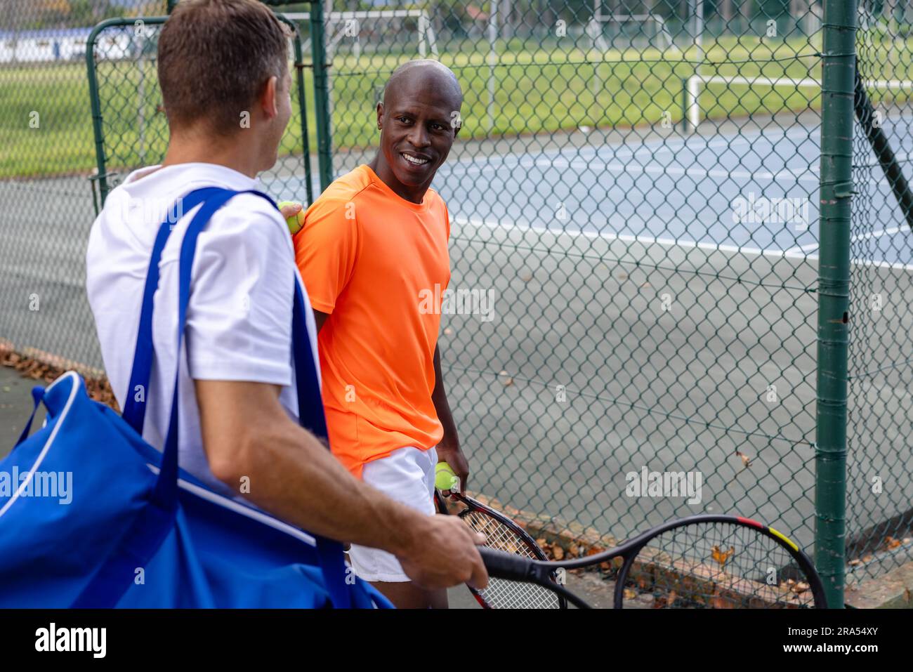 Happy diverse male tennis players with sports bag and rackets talking ...