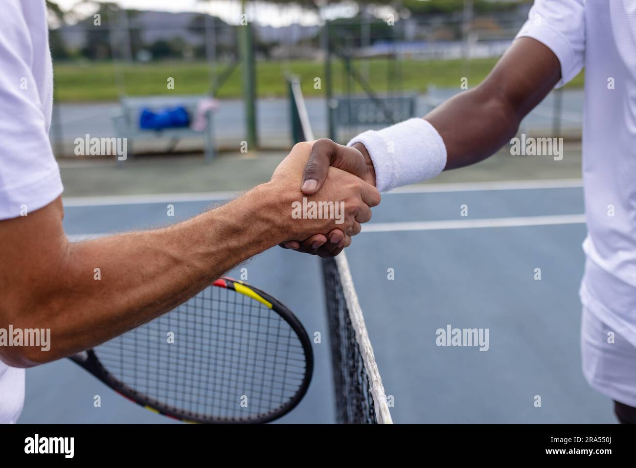 Hands of diverse male tennis players shaking hands on outdoor tennis ...